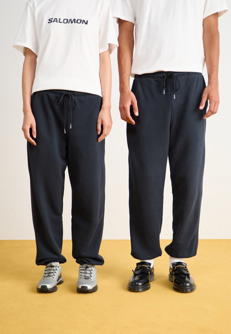 Salomon LOGO PRIDE JOGGER UNISEX - Tracksuit bottoms - deep black/black ...